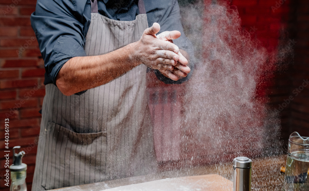 man in an apron take flour and clap their hands. scatter the flour ...