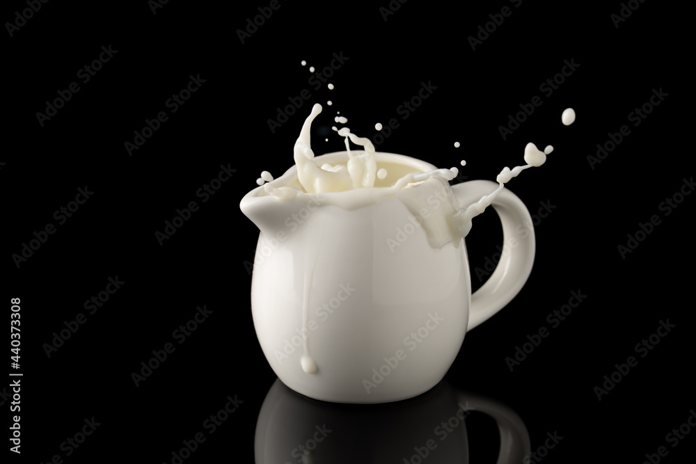 full jug of milk and splashing milk from it isolated on black ...