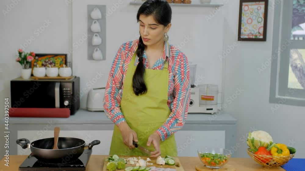 An Indian lady chopping the vegetables while stirring the food in the ...