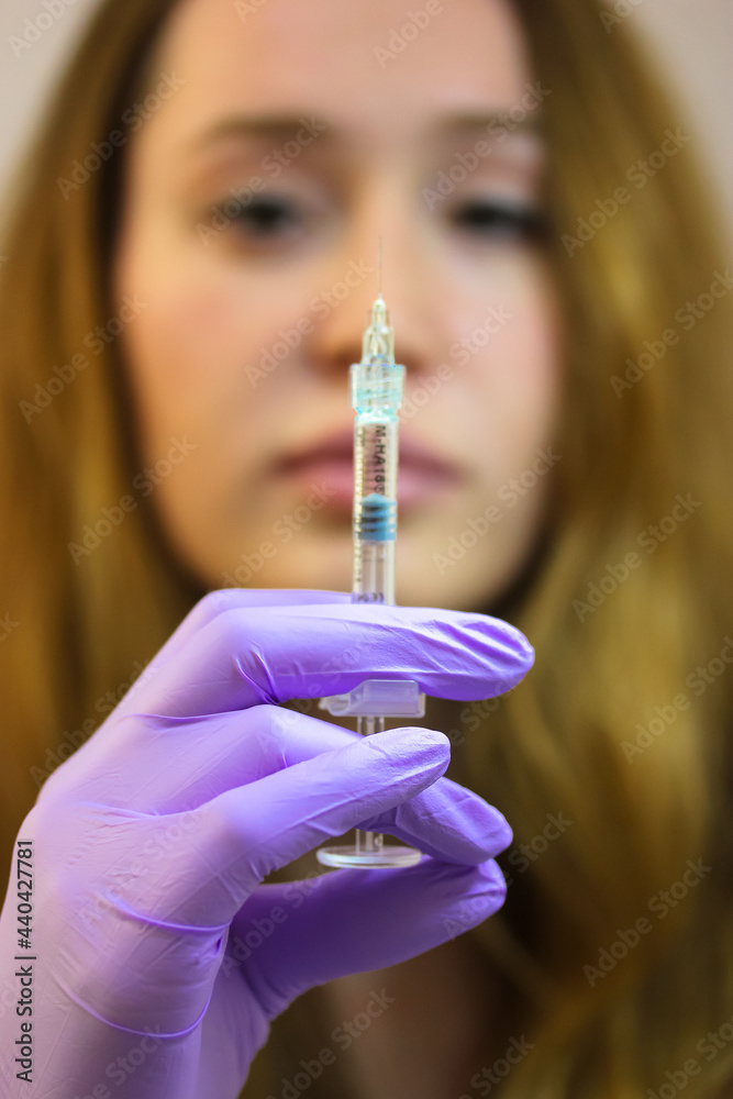 A young woman doctor wearing purple rubber gloves holds an injection ...