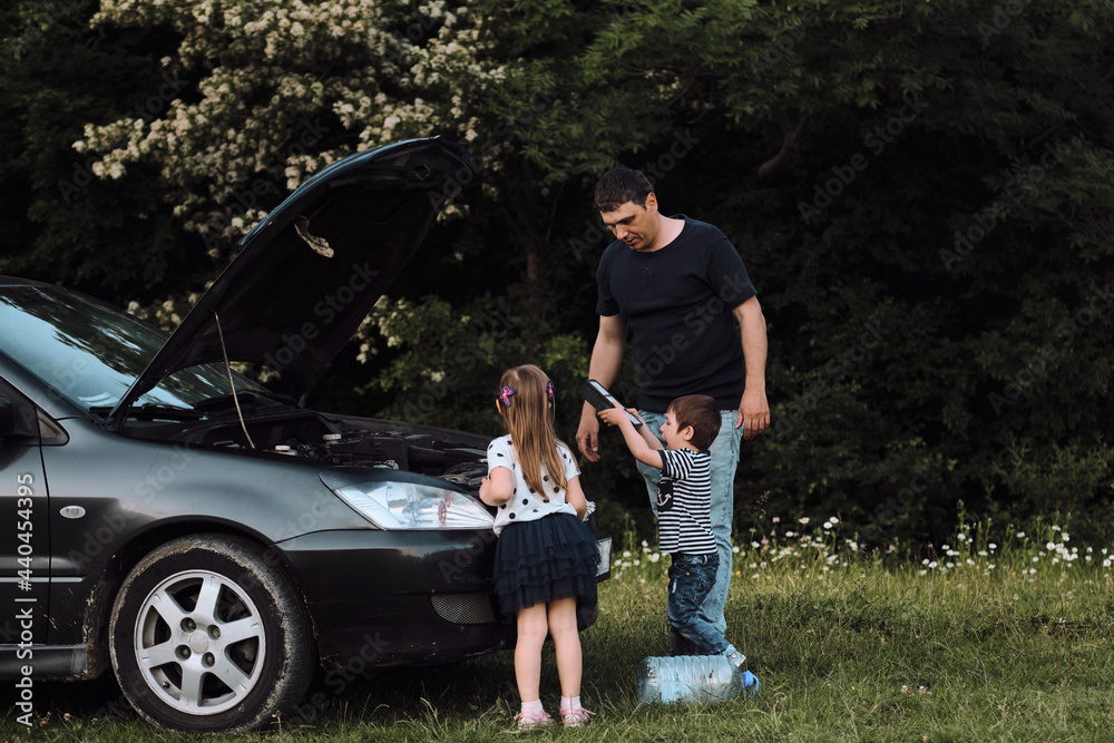 Father opened the hood of car and shows children engine and spare parts ...