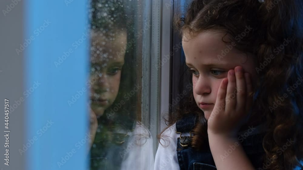 Close up of sad upset little kid sitting on windowsill sad to look away ...