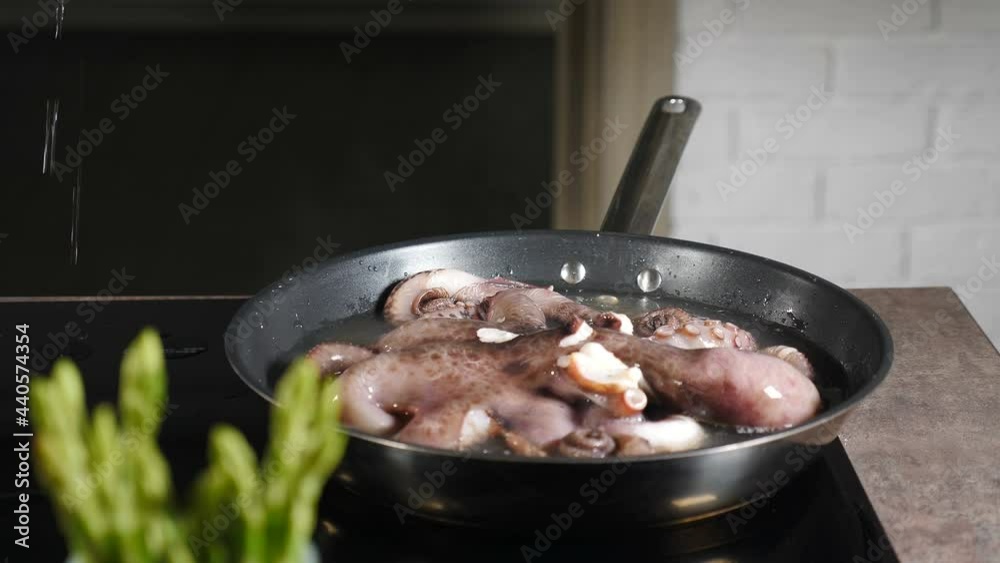 Pouring water into hot frying pan with boiling octopus. Boil liquid ...
