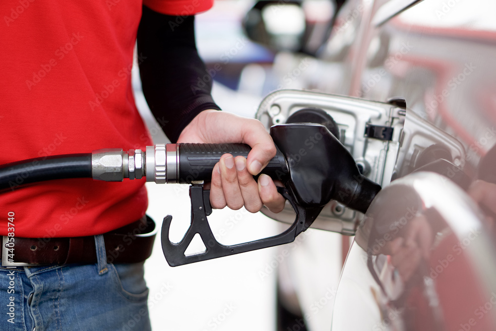 Gas station worker in red uniform filling up bronze pickup truck tank ...