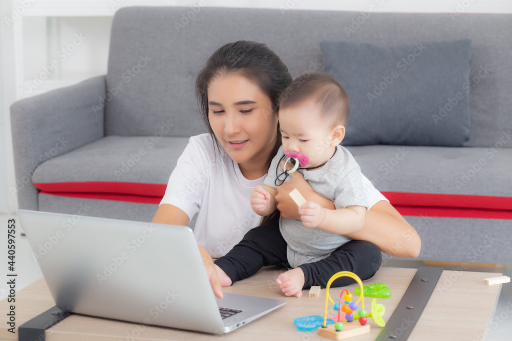 Young asian mother working on laptop computer while care daughter girl ...