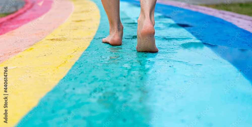 Female feet close up on barefoot on wet asphalt drawn rainbow walking ...