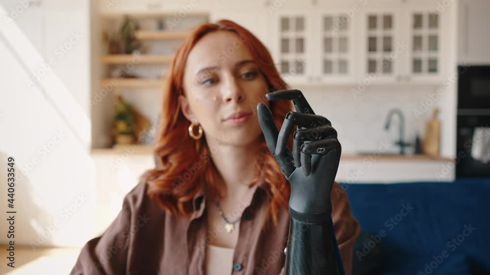 Young red-haired woman looks at her bionic prosthetic left hand and ...