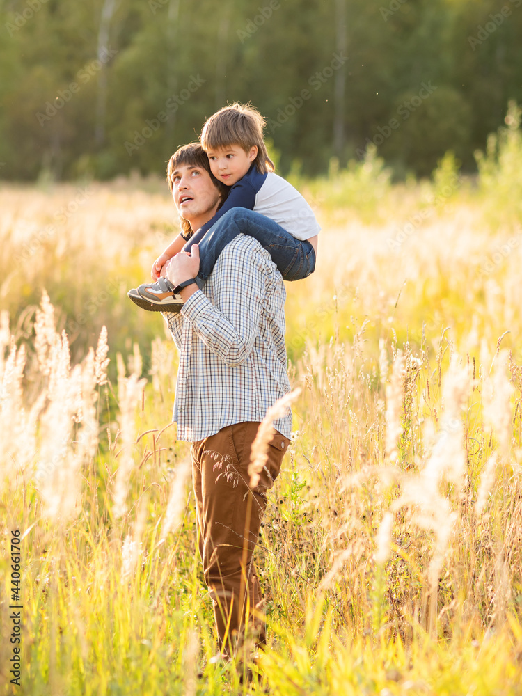 Father carries his son on shoulders. Family time outdoors. Man with ...