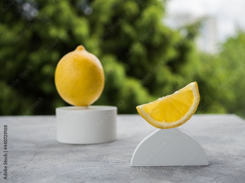 Still life concept: a slice of lemon and a whole lemon on a gray stand ...