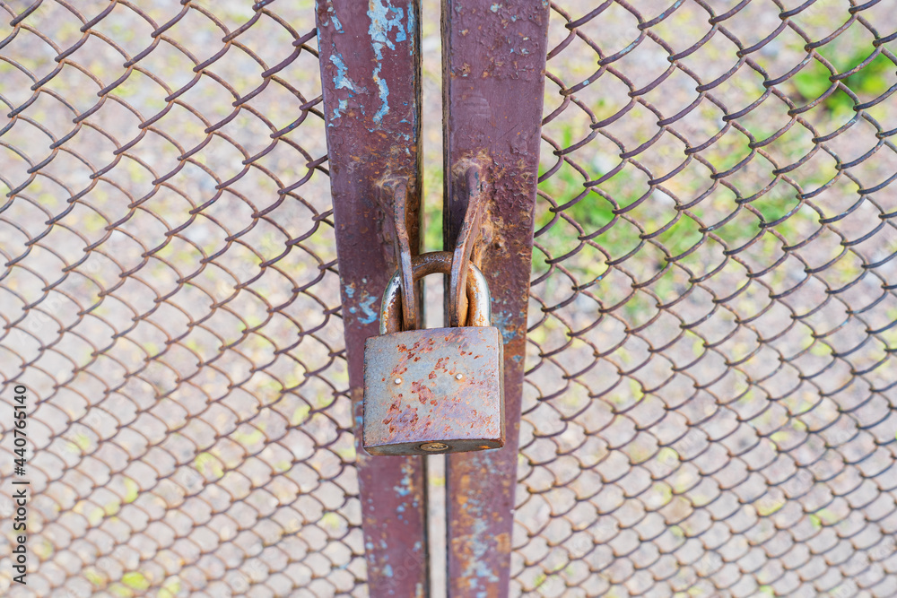 The old mesh gate is closed with a metal padlock. There are traces of ...