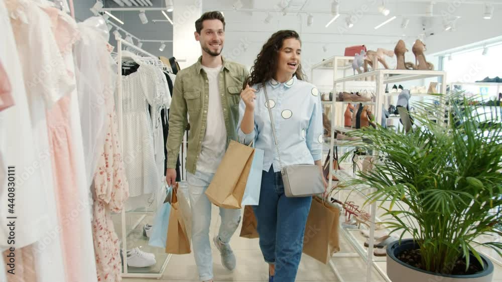 Cheerful man and woman walking in clothes store holding bags talking ...