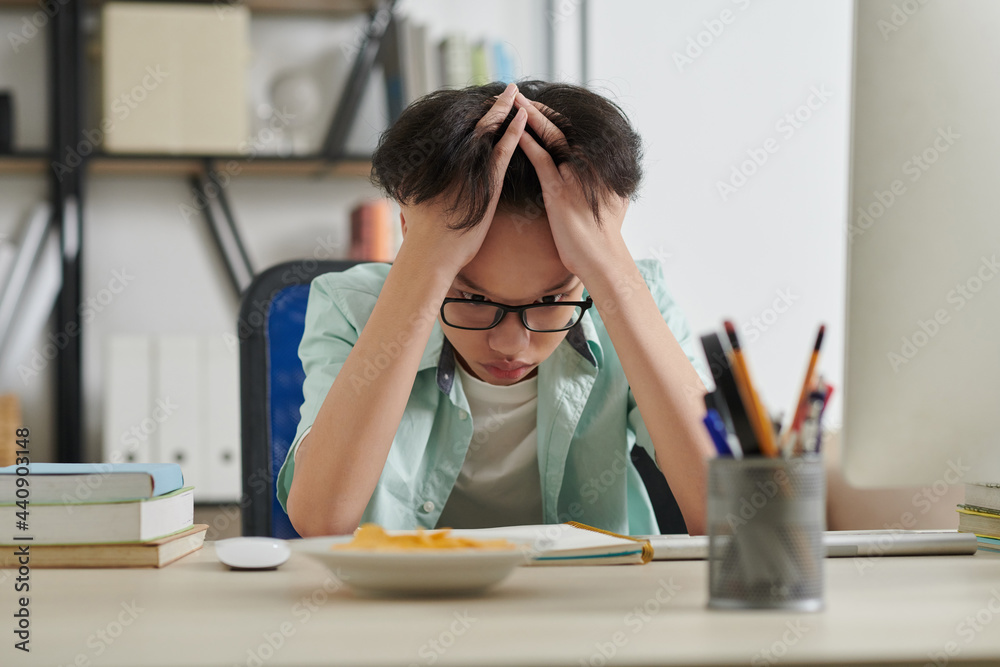Confused schoolboy looking at his textbook with hard equation he needs ...