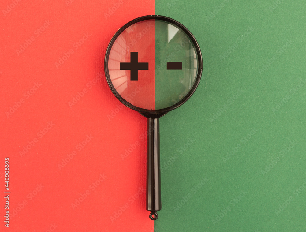 Plus and minus signs through magnifier on red and green background ...