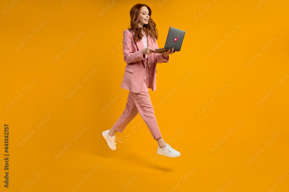 Red haired woman run jump typing laptop wearing elegant pink suit ...