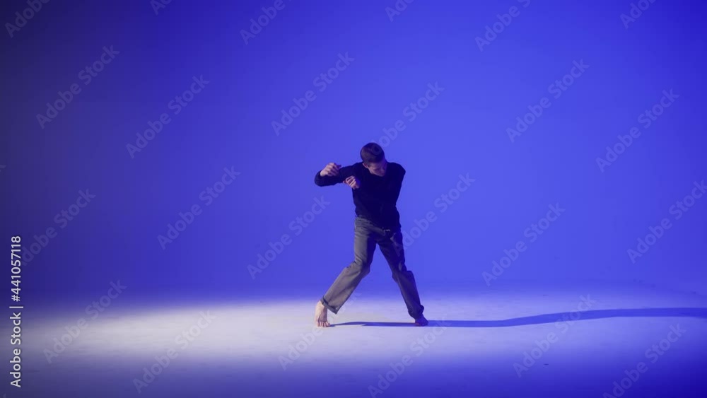 Talented barefoot man dancing contemporary on blue neon background in ...