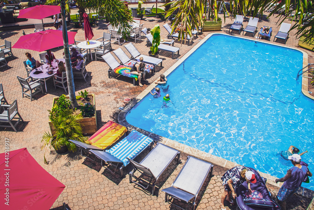 Resort swimming pool with kids in floatys and people lounging on chiars ...