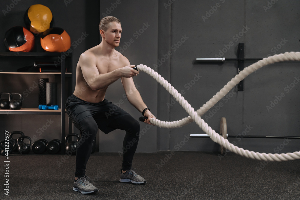 Muscular shirtless man working out with heavy battle ropes at crossfit ...