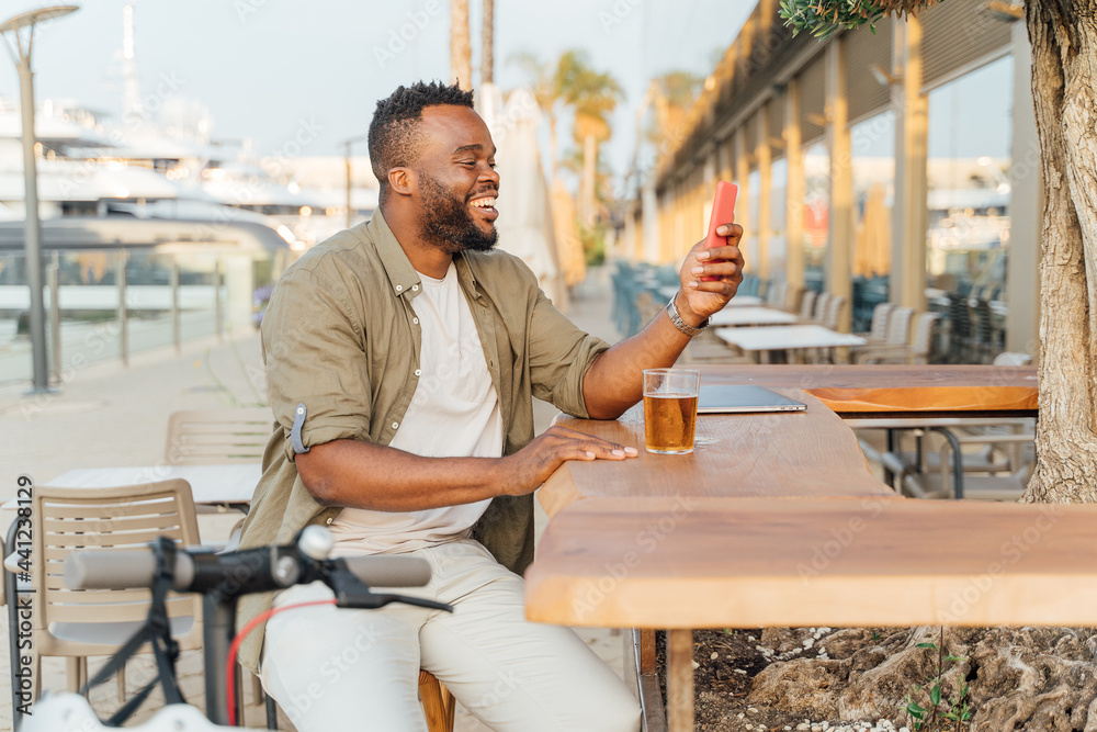 African man drinking a beer after work while making a video call at ...