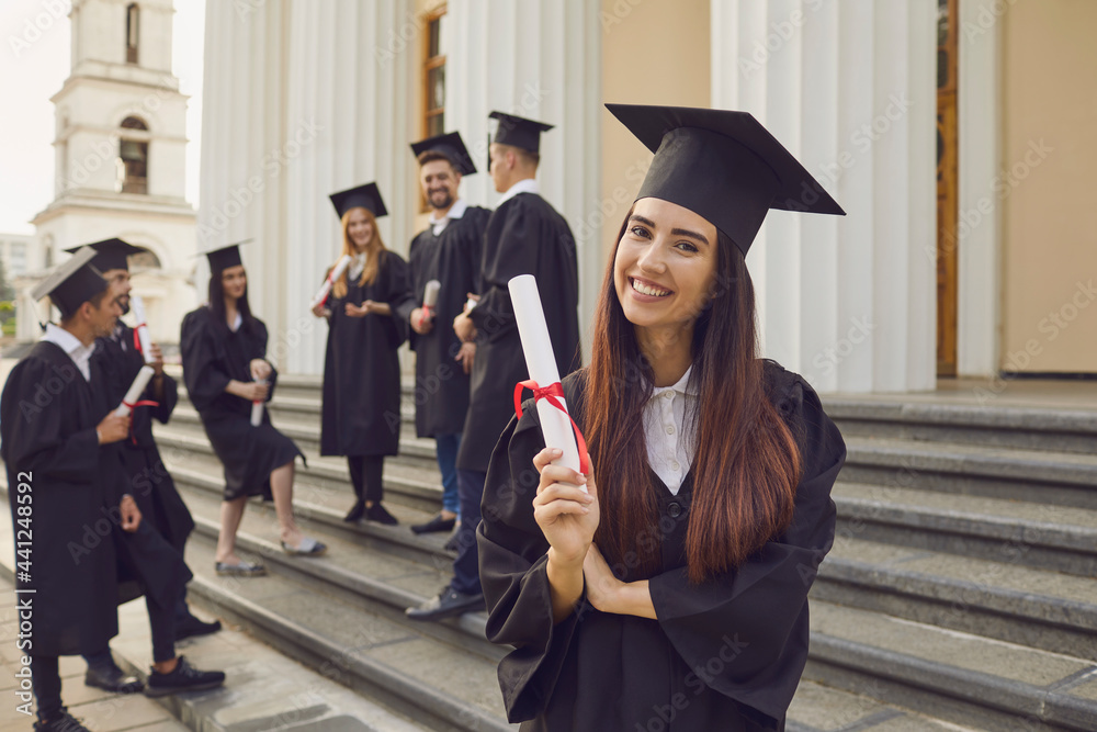 Happy positive pretty girl university graduate standing holding diploma ...