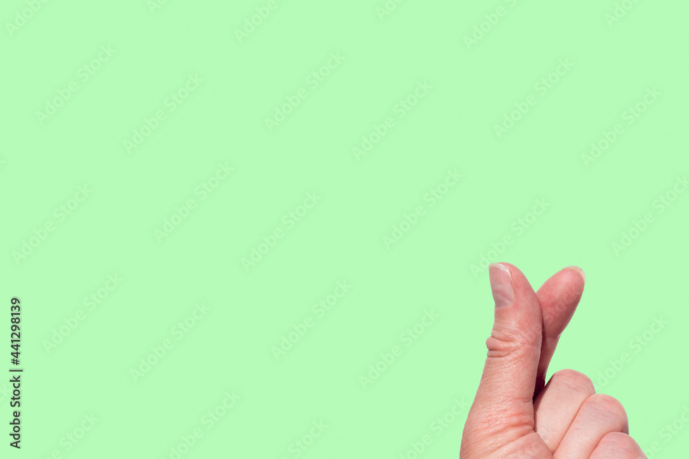 A hand making a heart shape with two fingers on a mint green background ...