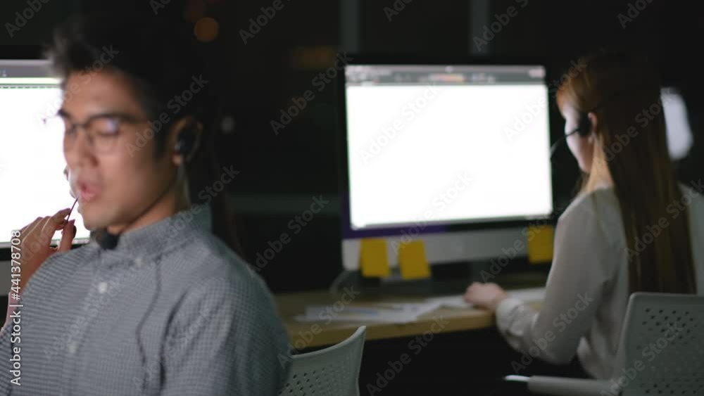 Pan shot of call center team work together at night to support the ...