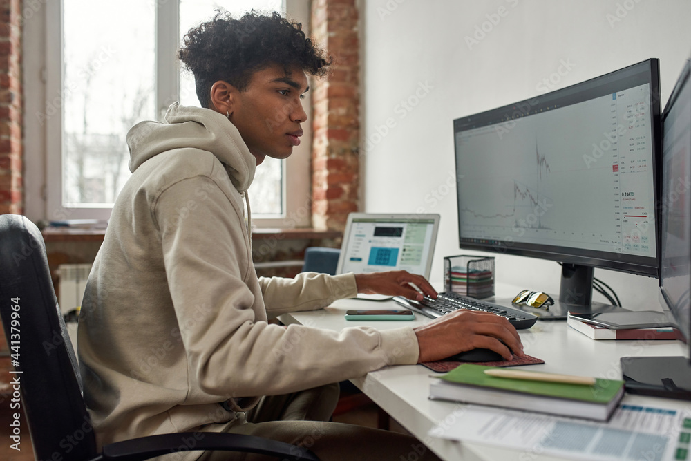 Focused young man looking at pc screen while trading online using ...