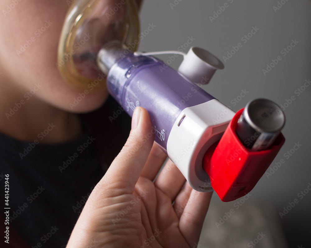 Young boy using asthma inhaler with help from parent; a spacer is used ...