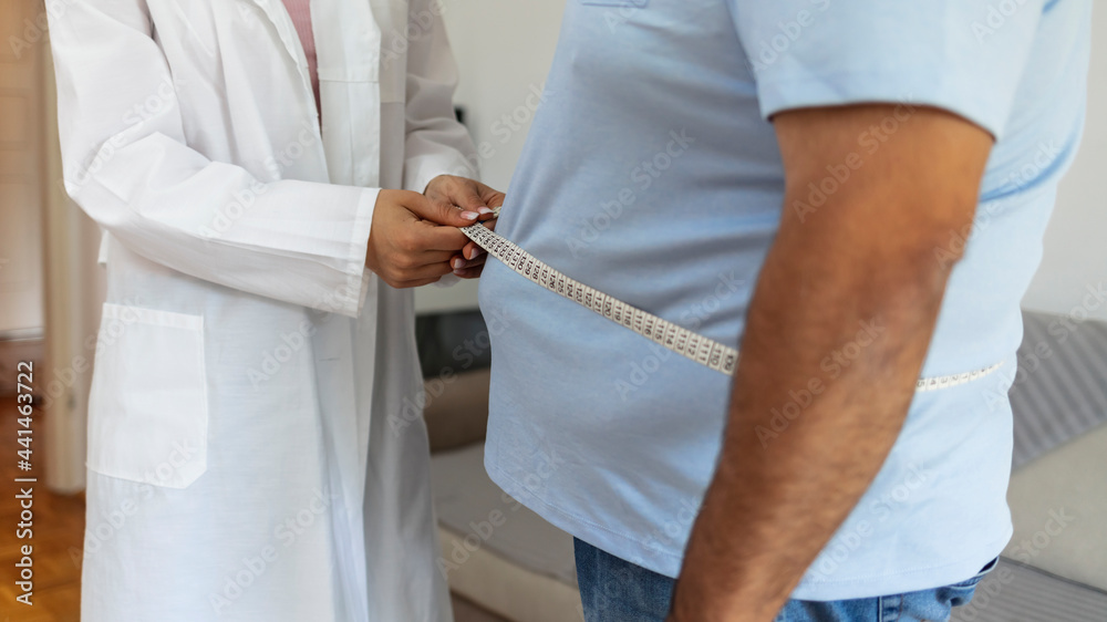 Shot of a young female doctor using a tape measure to measure the waist ...