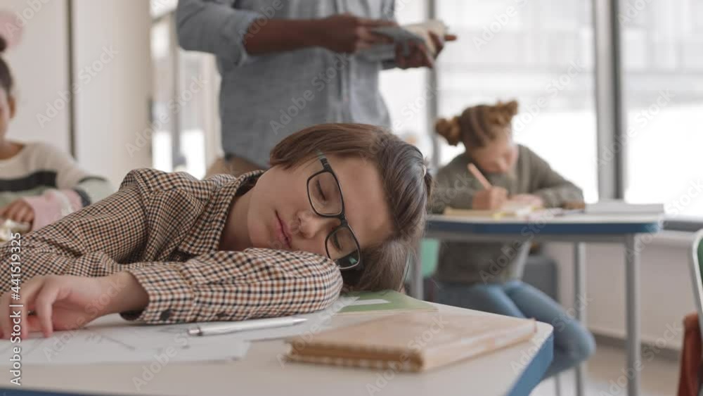PAN medium close-up with slowmo of teenage school boy napping on desk ...