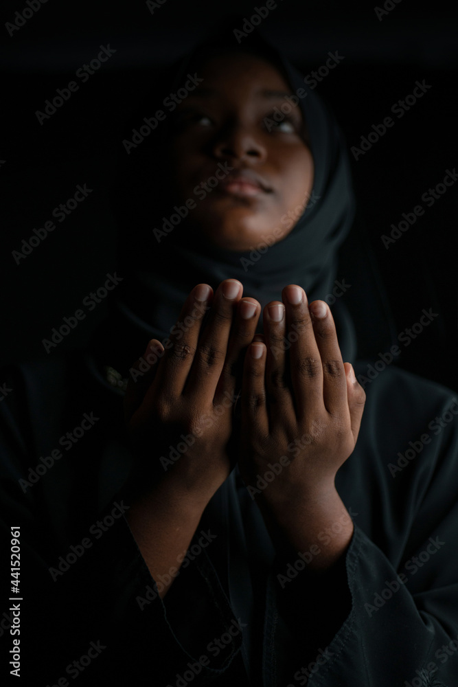 Dark skinned Muslim girl in black hijab, doing prayers on black ...