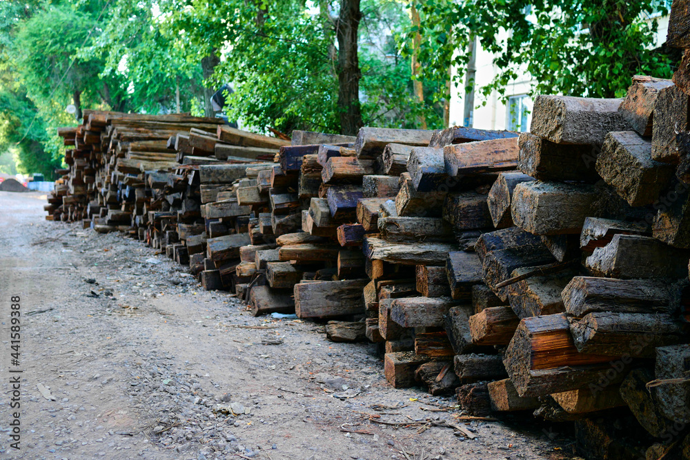 A large pile of wooden sleepers in the daylight. A row of wooden bars ...