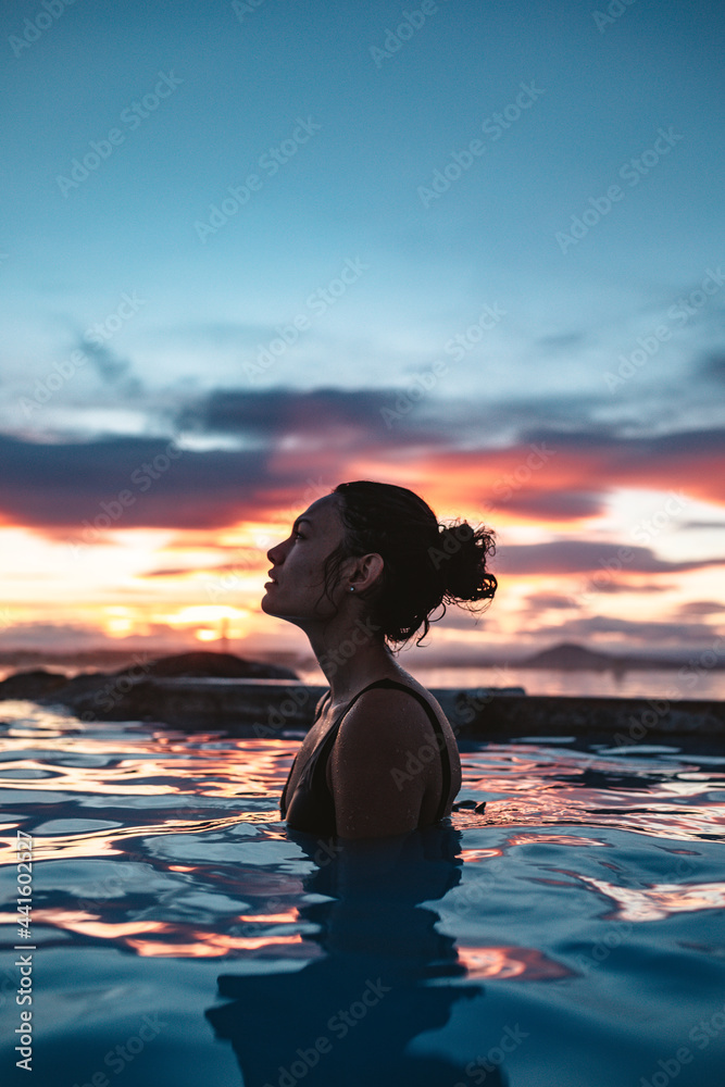 Side view of young woman in swimsuit posing in blue water between rocks ...