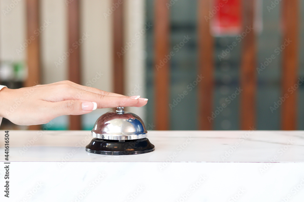 Closeup of hand ringing silver bell on hotel reception service desk ...