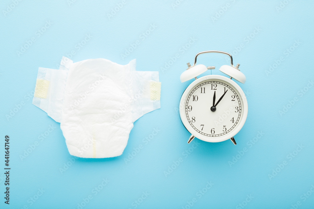 Alarm clock and white soft new baby diaper on light blue table ...