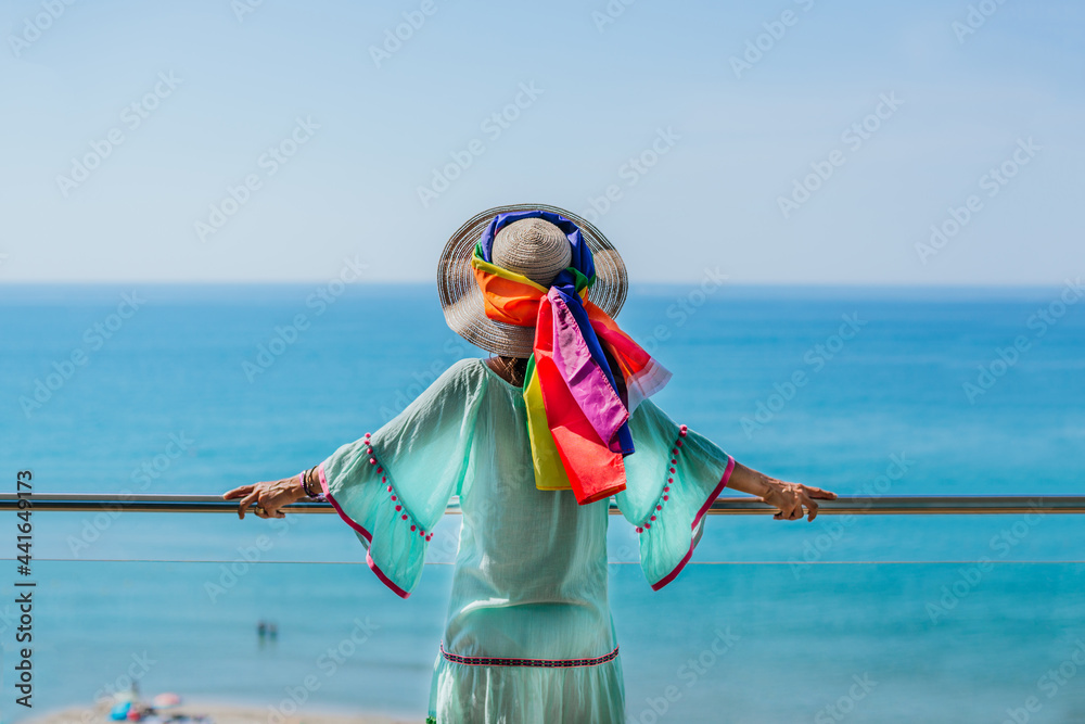 woman with her back to the sea in summer. she is leaning on a steel ...