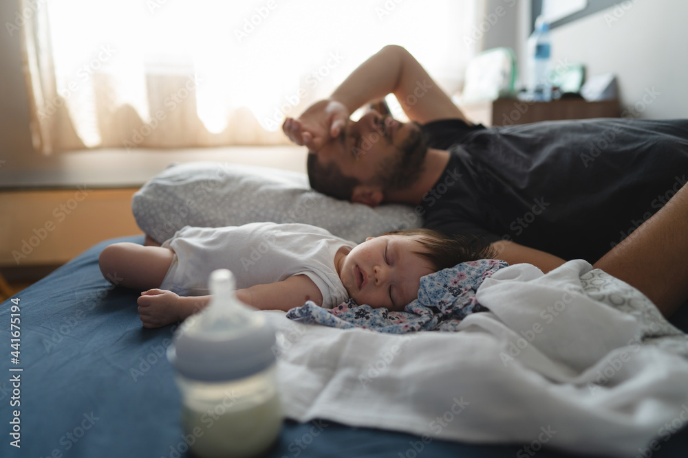 Foto de Exhausted man father lying by his three months old baby on the ...