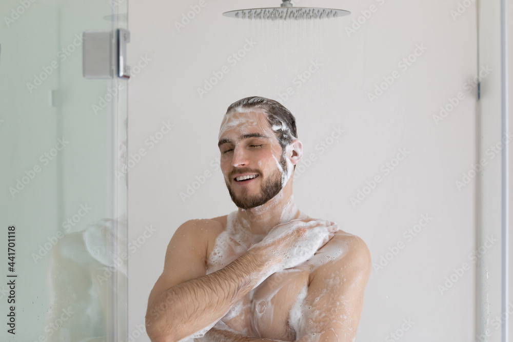 Happy relaxed handsome well built guy in soap gel foam standing under ...