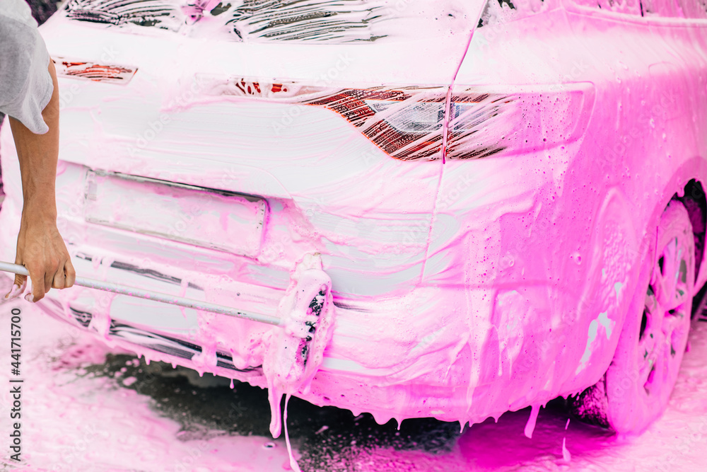 Car wash concept, Front view of white sports car covered with pink foam ...