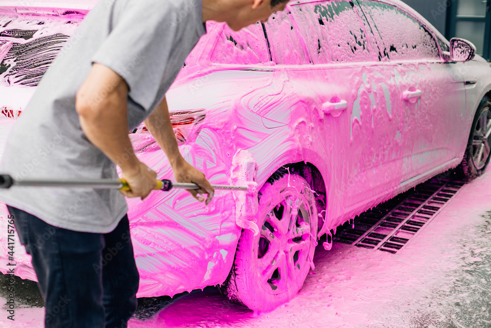 Car wash concept, Front view of white sports car covered with pink foam ...