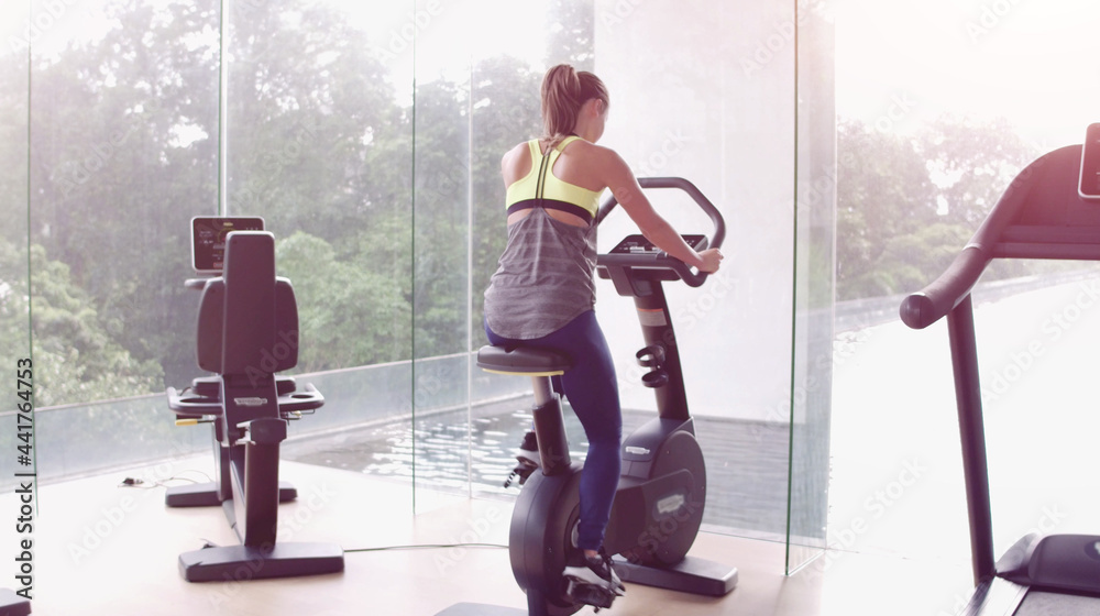 Back view of attractive woman at the gym riding on the spinning bike ...