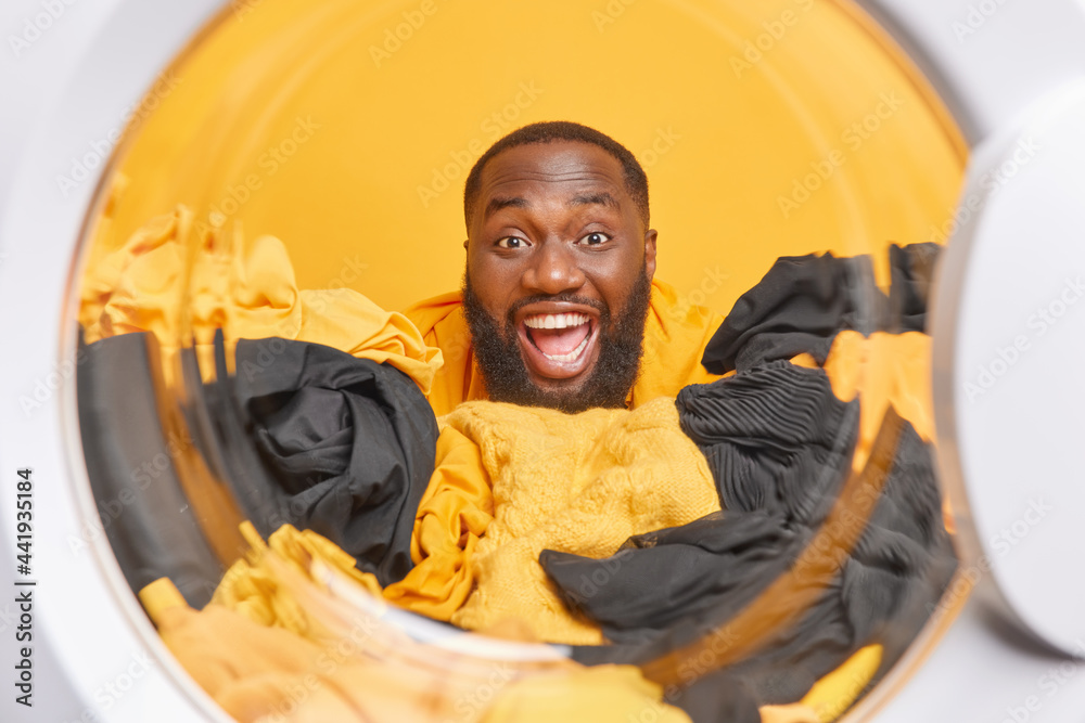 Positive black adult man poses through washing machine drum has happy ...
