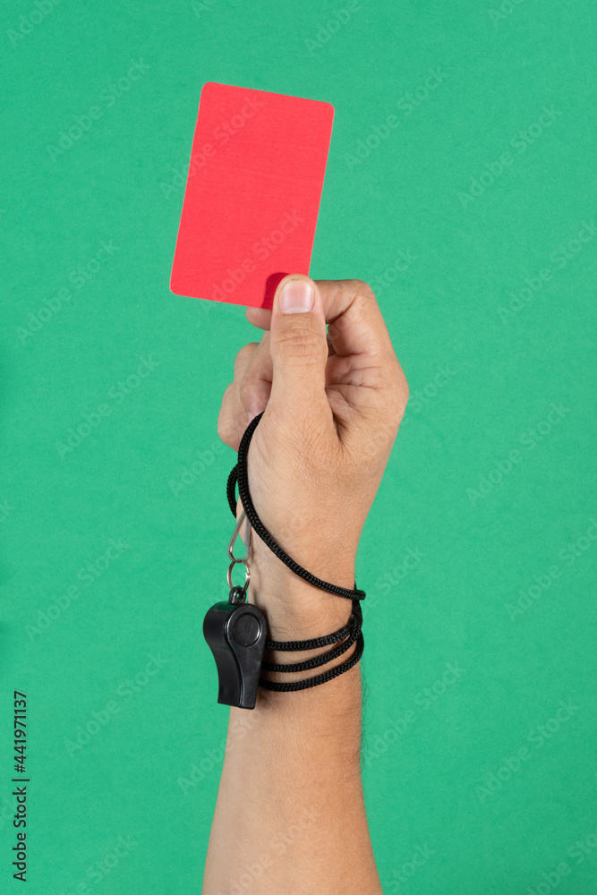 referee's hand holding a red card and whistle on green background ...