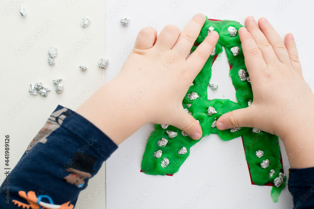 Two year boy decorating play dough letter "A "with aluminum foil balls ...