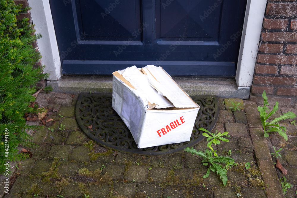 Damaged delivery cardboard box at front door of a house, Fragile ...