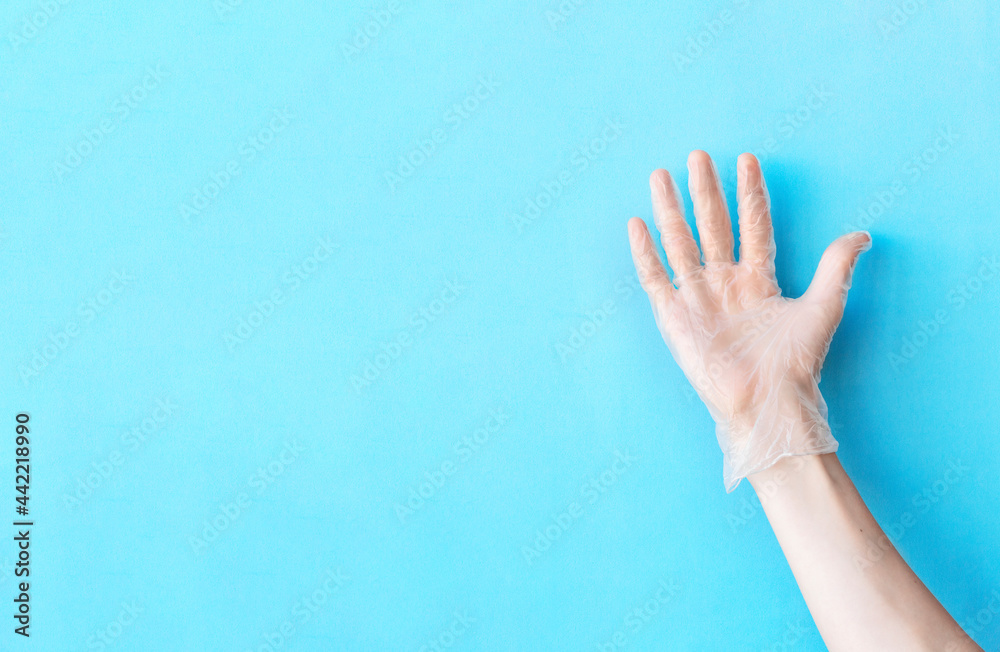 Human hand in transparent vinyl glove raised above light blue ...