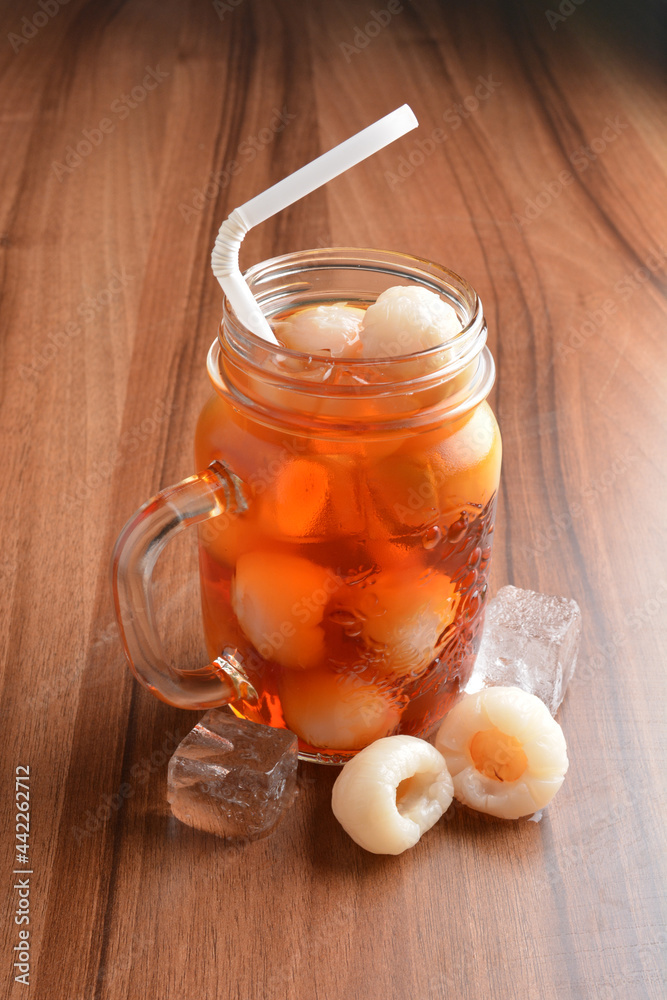 cold lychee longan fruit ice tea kombucha with white straw on wood ...
