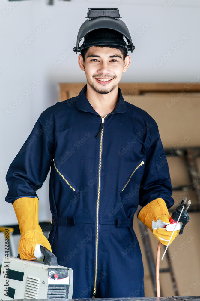 Happy young Asian male welder holds welding torch at workplace ...