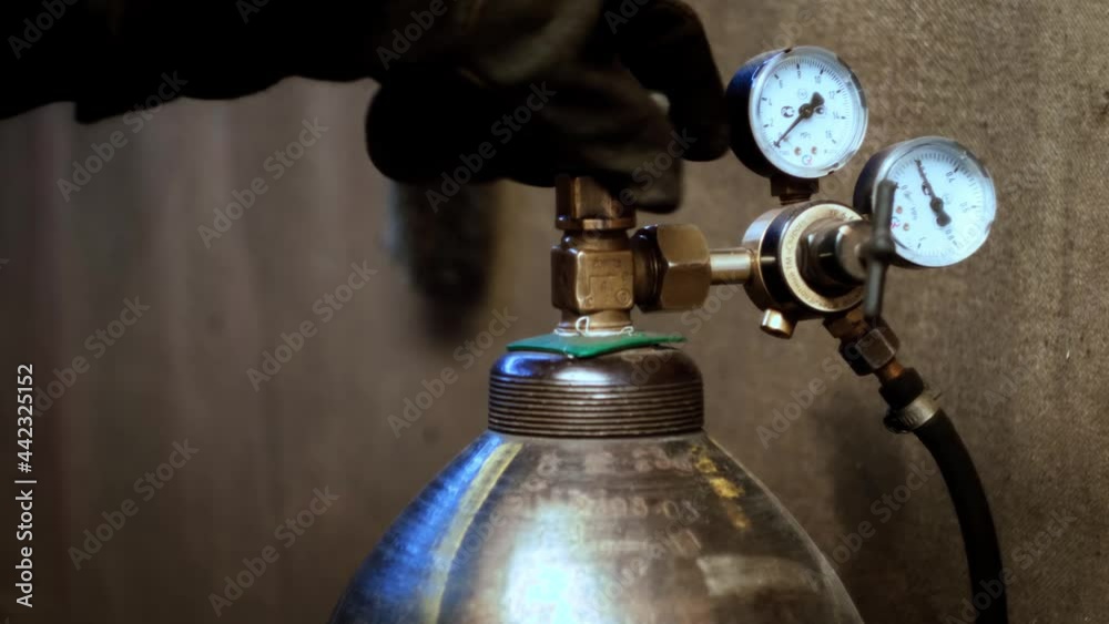 A welder in protective gloves opens a gas cylinder valve with pressure ...