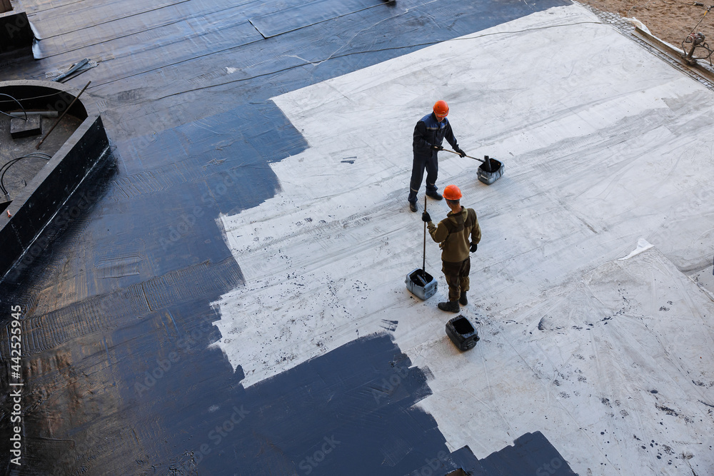 Waterproofing coating. A worker applies bitumen mastic to the ...