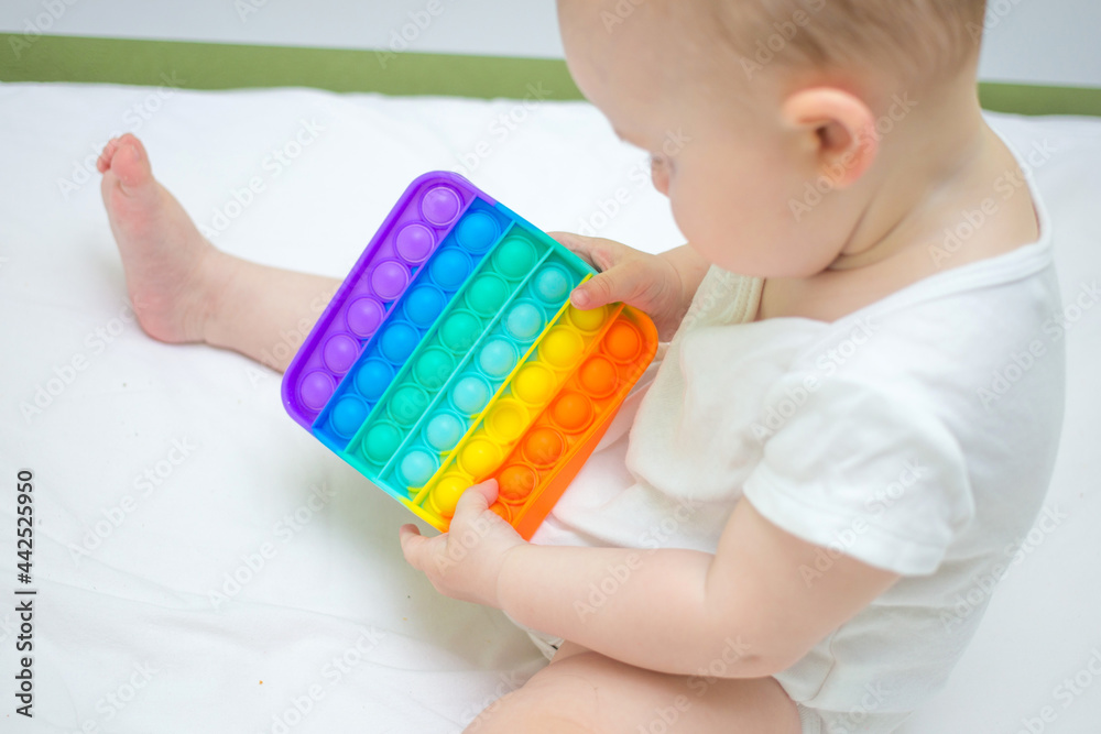 Little baby girl sitting at home on the bed, playing Pop-it new anti ...